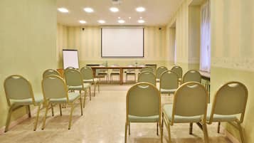 Uma sala de conferências com uma mesa comprida, várias cadeiras, uma tela de projetor e uma lousa.