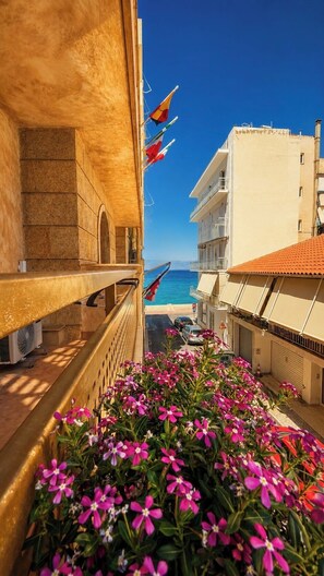 Uma varanda com vista para o mar, um edifício com varandas e um canteiro com flores cor-de-rosa.
