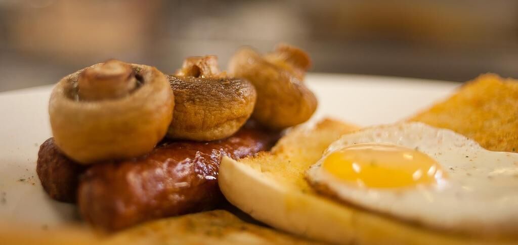 Prato de café da manhã com salsichas, cogumelos, torradas e um ovo frito.