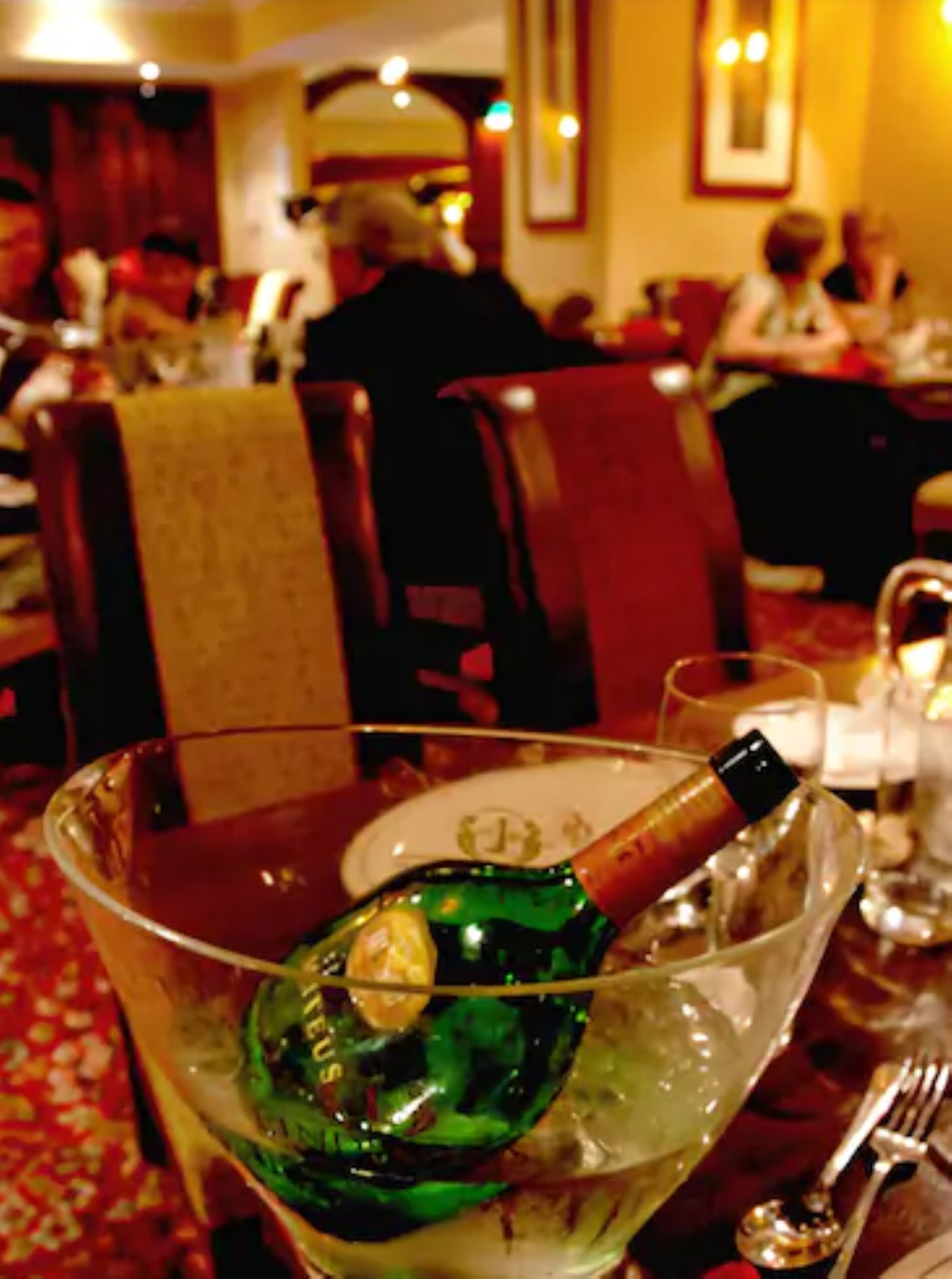 Uma área de bar com um copo contendo uma garrafa de bebida, uma mesa de jantar com cadeiras e uma pessoa ao fundo.