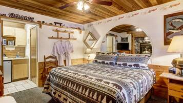 Quarto aconchegante com teto de madeira, cama com roupa de cama estampada, um espelho e uma pequena escrivaninha com abajur.