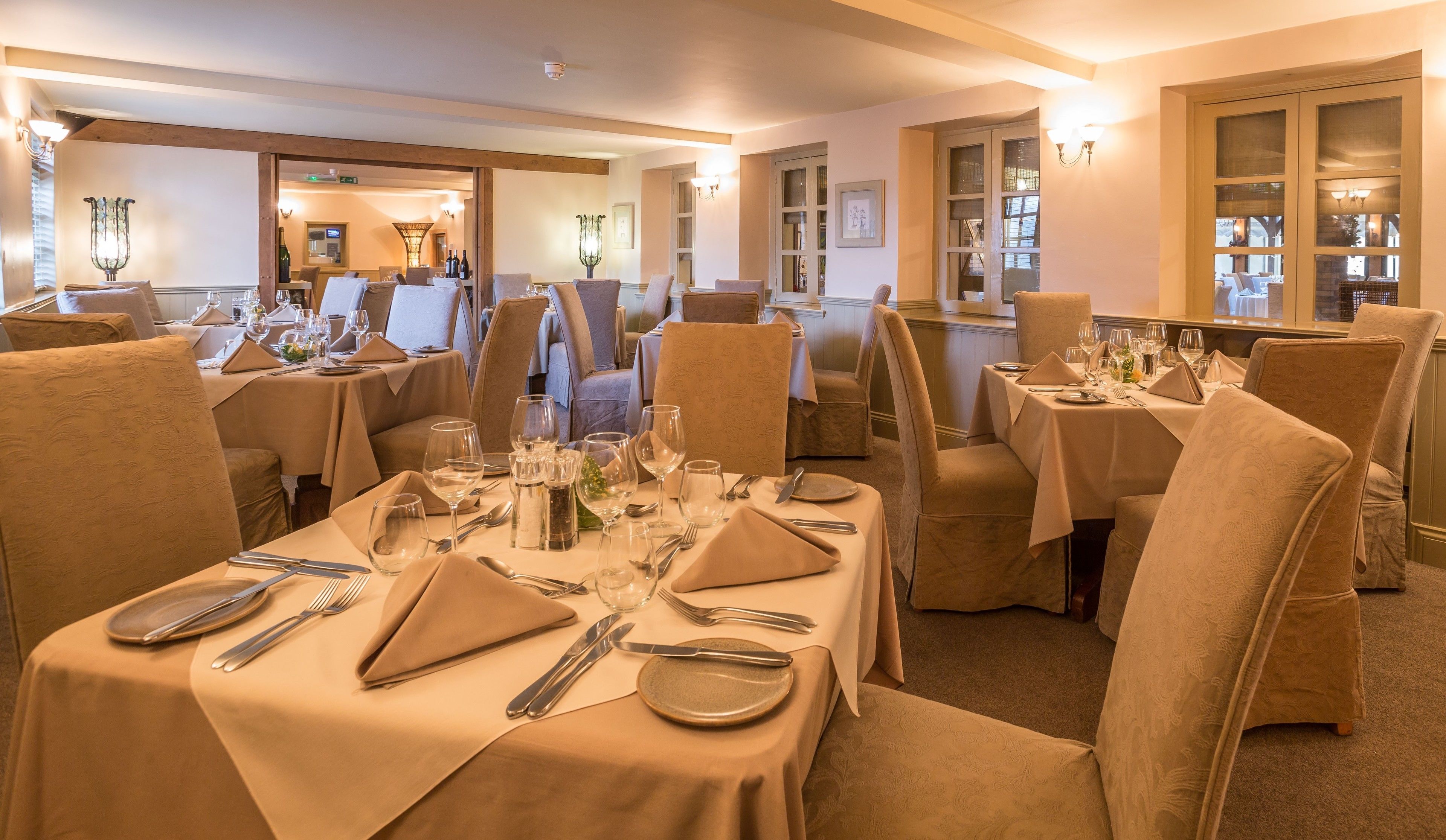 Restaurante com mesas preparadas para refeições, com toalhas de mesa bege e cadeiras combinando.