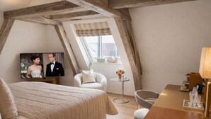 Quarto com cama, televisão, cadeira, mesa pequena e janela.