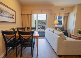 Sala de estar com sofá, mesa de jantar e cadeiras, varanda com vista e luminária.