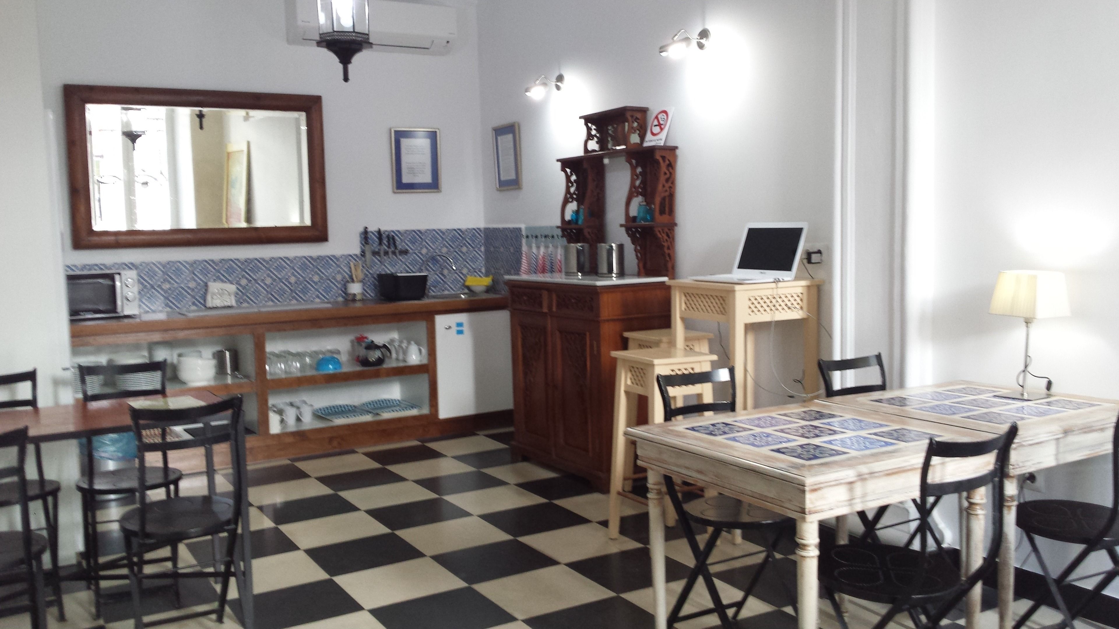 Uma cozinha com piso xadrez, armários de madeira, micro-ondas, pia e uma mesa de jantar com cadeiras.