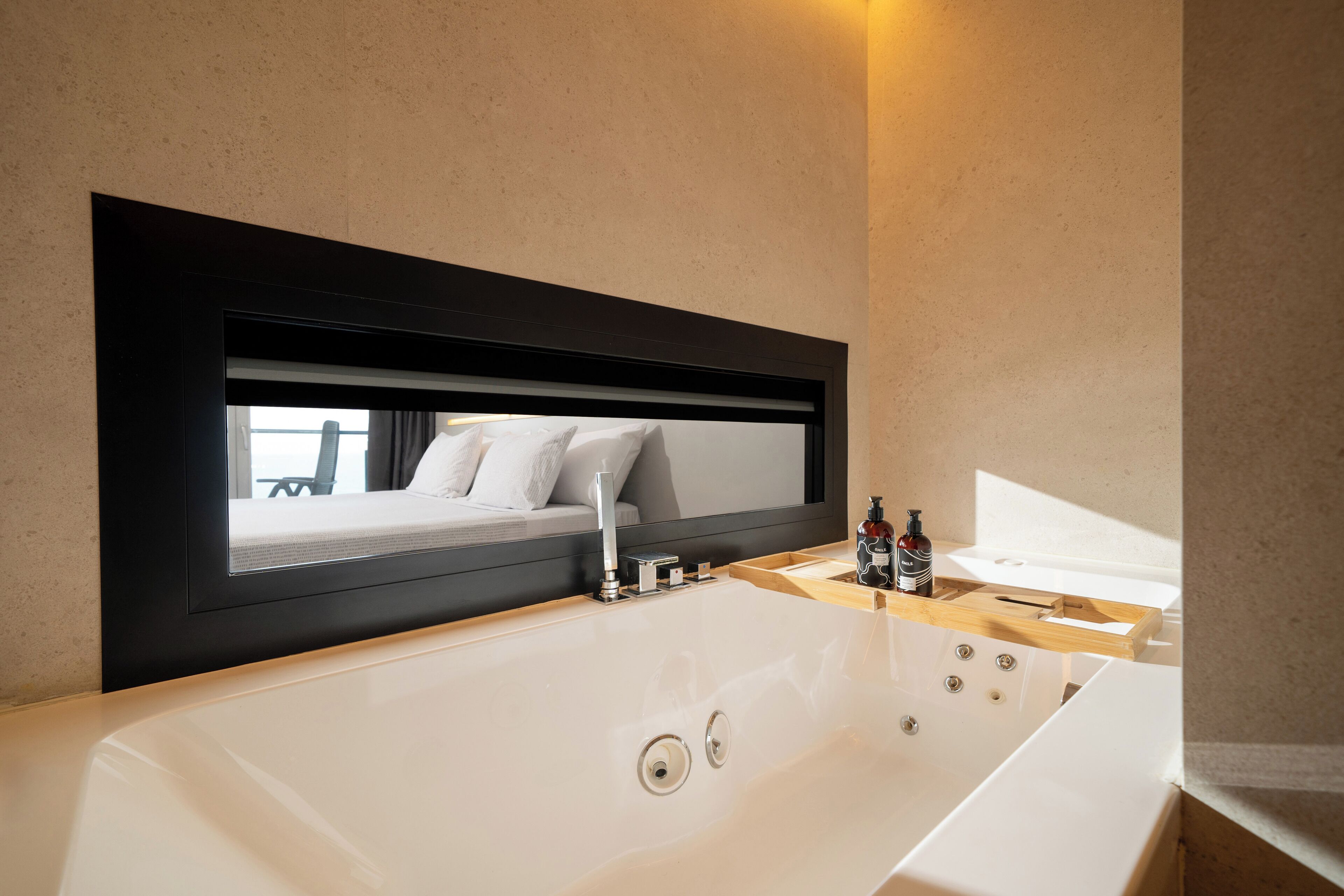 Um banheiro moderno com uma banheira grande, um espelho sobre a pia e vista para um quarto refletida no espelho.