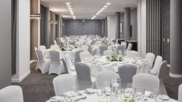 Salão de banquetes com mesas redondas preparadas para refeições, cadeiras brancas e uma paleta de cores neutras.