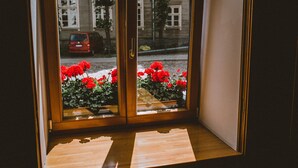 Janela de madeira com vista para flores vermelhas e um carro vermelho lá fora.