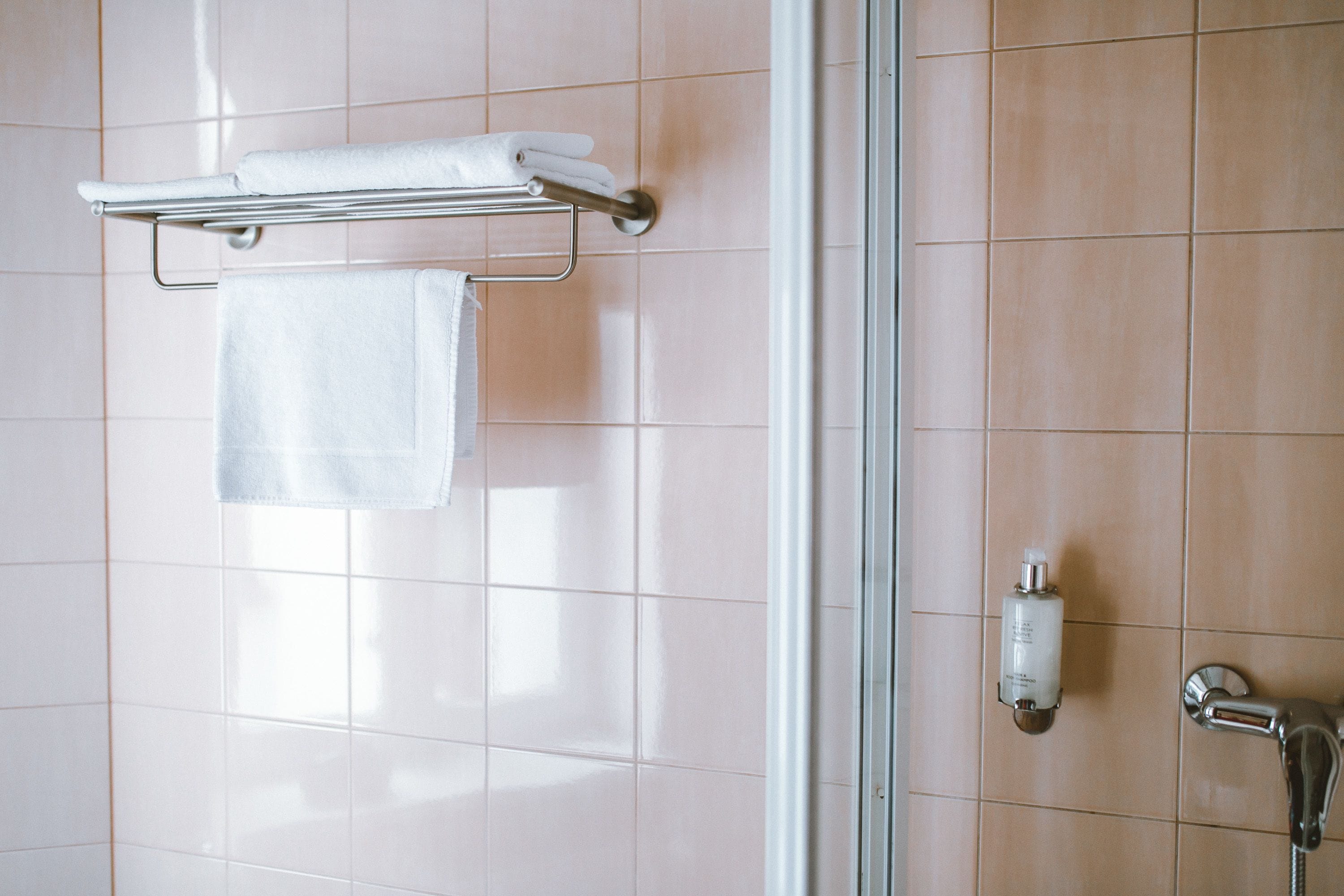 Um banheiro com porta de vidro para o chuveiro, um porta-toalhas com duas toalhas e um dosador de sabonete na parede.