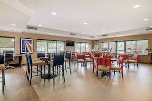 Uma sala de conferências ampla, com várias mesas e cadeiras, janelas grandes e uma televisão de tela plana na parede.