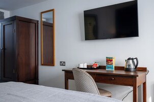 Quarto de hotel com cama, escrivaninha, cadeira, televisão, guarda-roupa e espelho.