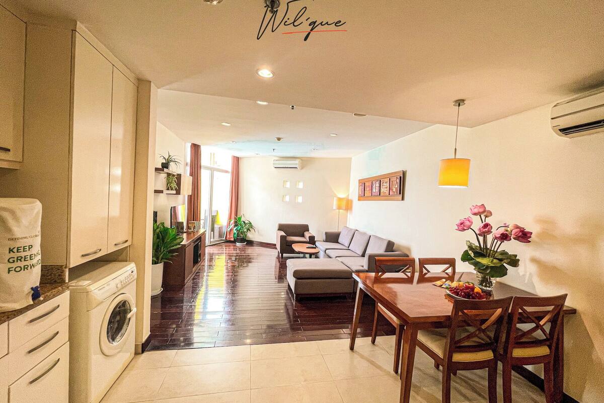 Uma sala de estar moderna com sofá, mesa de jantar com cadeiras e área de cozinha com máquina de lavar.