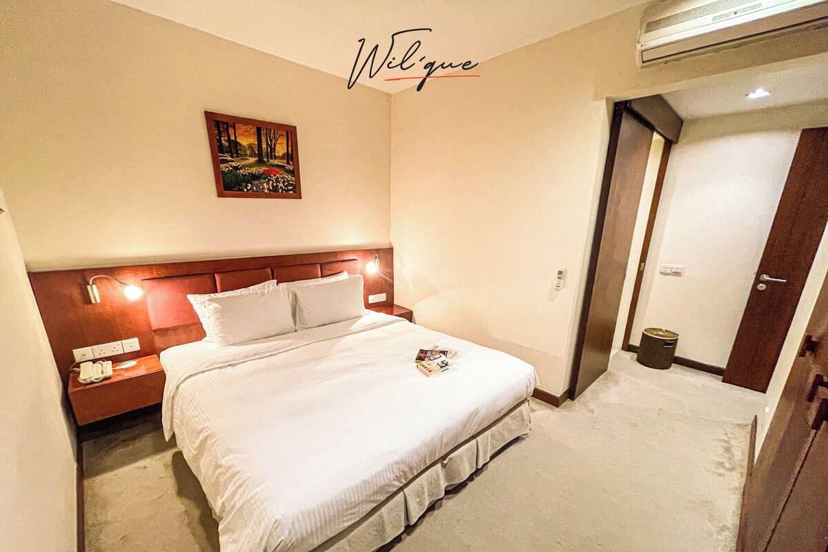 Quarto de hotel com cama, mesa de cabeceira, quadro na parede e porta.