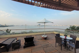 Um deck com móveis de vime, uma mesa com planta em vaso e vista da linha do horizonte da cidade através da água.