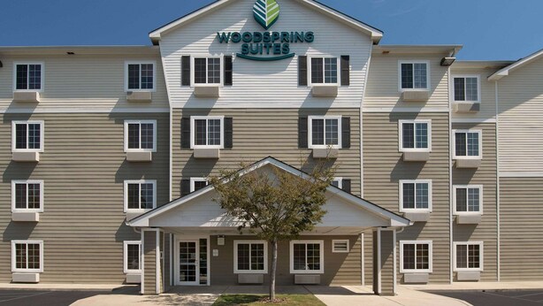 Um hotel de vários andares com entrada central e uma placa com a inscrição 'Woodspring Suites'.