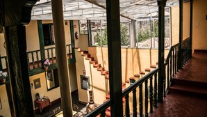 Um interior amplo com escada que leva a um andar superior, área coberta com vista para o exterior e design tradicional com grades e colunas de madeira.