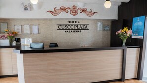 Uma receção de hotel com balcão de madeira, uma cadeira preta e uma placa na parede com a inscrição "HOTEL CUSCO PLAZA NAZARENAS".