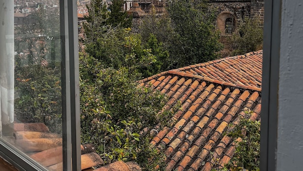 Vista da janela com um edifício histórico, um dome e torres sineiras, cercado por vegetação e uma paisagem montanhosa.