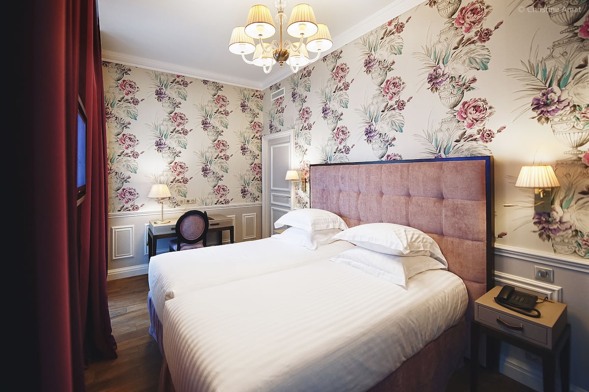 Quarto de hotel com uma cama grande, uma escrivaninha, uma cadeira e um telefone num criado-mudo.