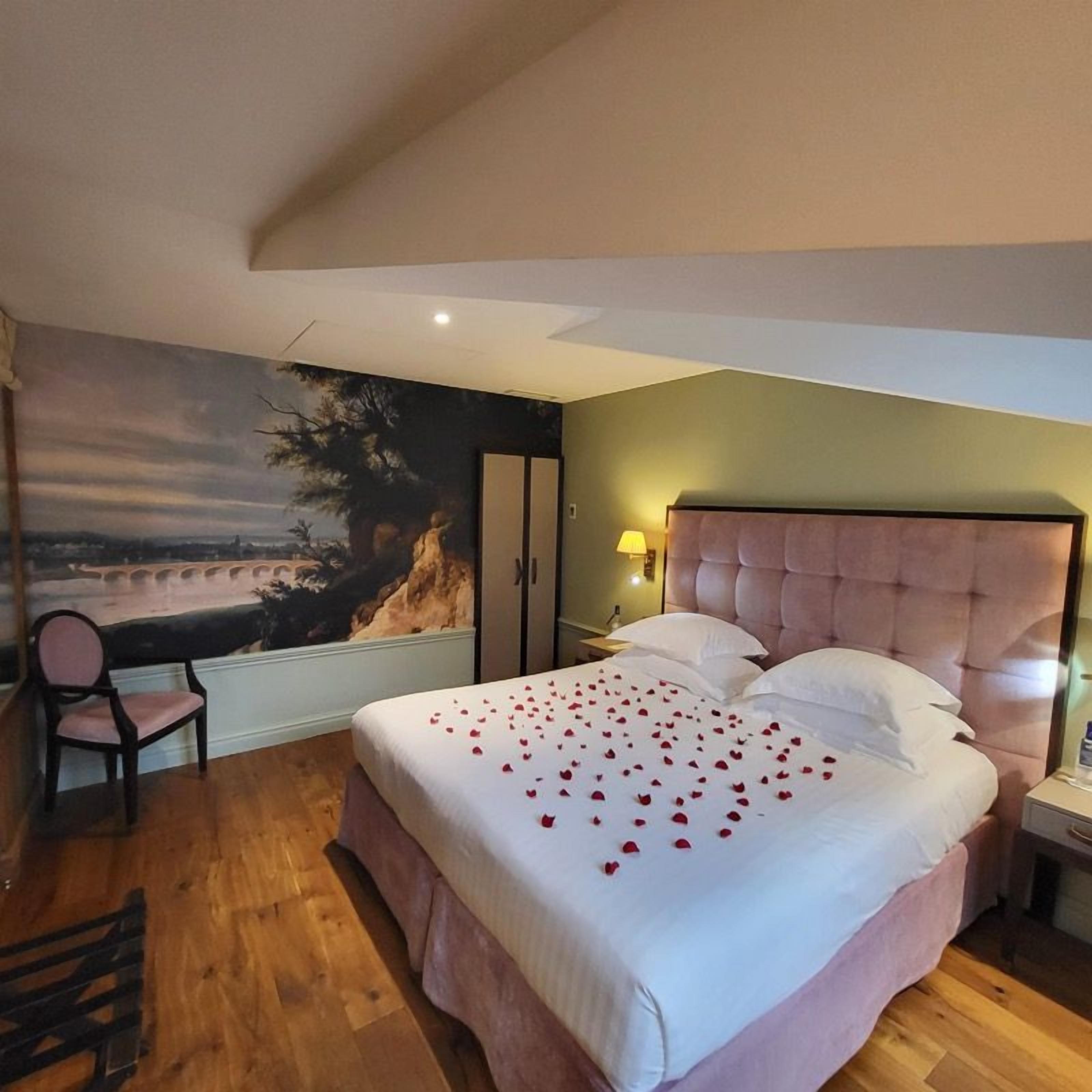 Quarto com uma cama grande, uma cadeira, uma escrivaninha e um mural na parede.