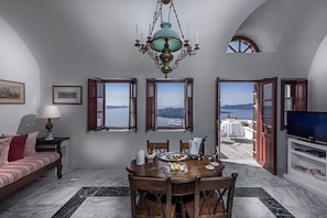Uma sala de jantar com vista para o mar, um lustre e uma televisão numa estante.