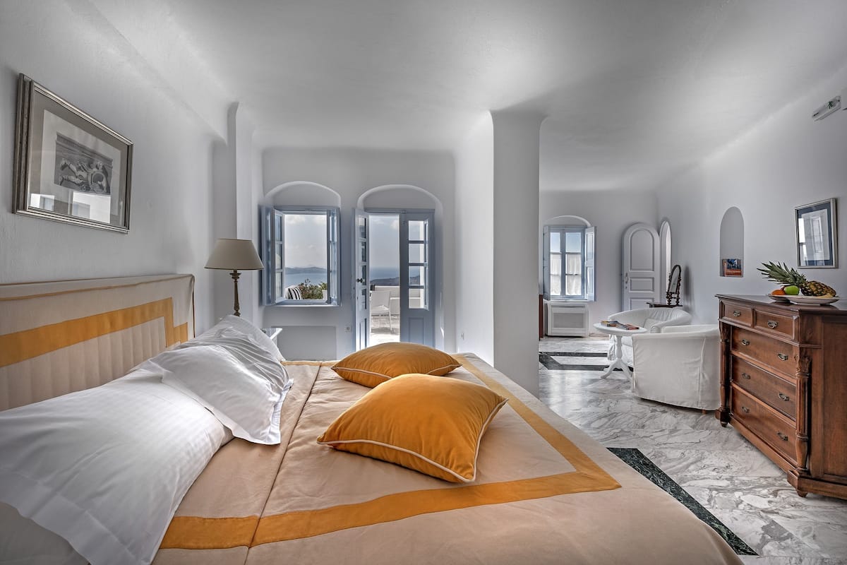 Um quarto espaçoso com uma cama grande, penteadeira de madeira e vista para o mar através de portas abertas.