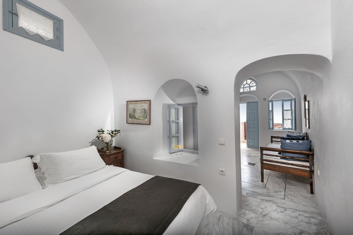Quarto com cama, mesa de cabeceira, janela e vista para outro cômodo.
