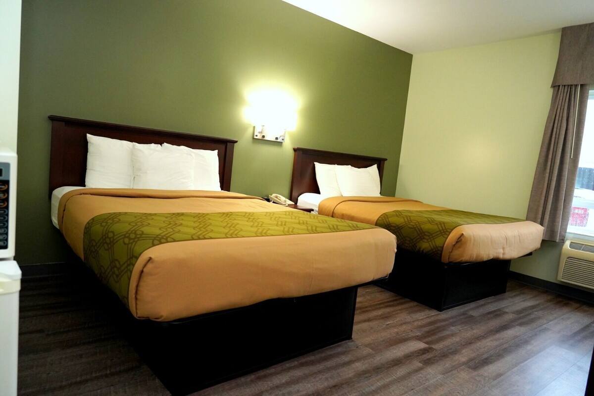 Quarto de hotel com duas camas, telefone ao lado da cama e janela com cortinas.