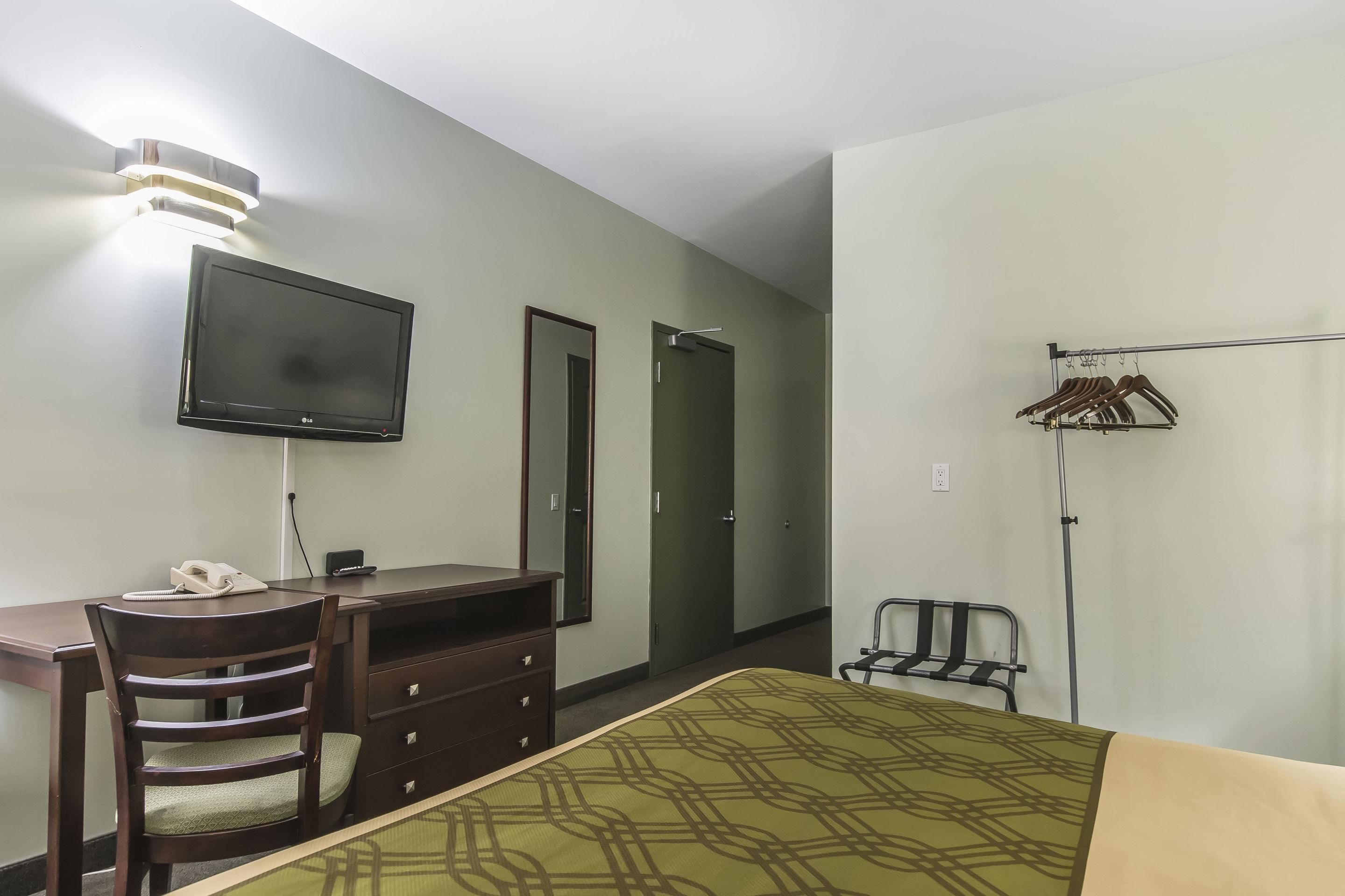 Quarto de hotel com escrivaninha, cadeira, cama, televisão, guarda-roupa e cabideiro.