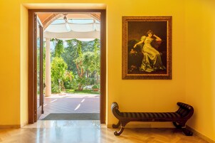 Quarto com um banco, uma pintura emoldurada e vista de um jardim por uma porta aberta.