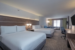 Quarto de hotel com duas camas, uma mesa, uma cadeira, uma televisão e uma janela com cortinas.
