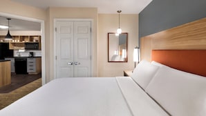 Quarto de hotel com cama, escrivaninha, micro-ondas e porta para a cozinha.