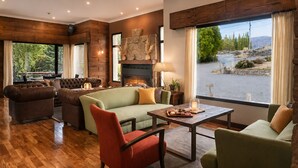 Sala de estar moderna com lareira, sofás de couro e vista para uma paisagem montanhosa.