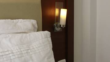 Quarto de hotel com uma cama bem arrumada, luminária na parede e uma tomada.