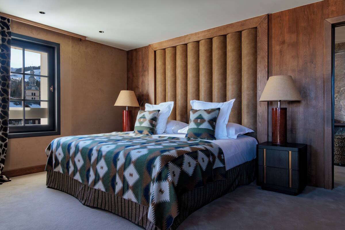 Quarto com cama grande, duas mesas de cabeceira com luminárias, uma janela com vista e cabeceira de madeira.