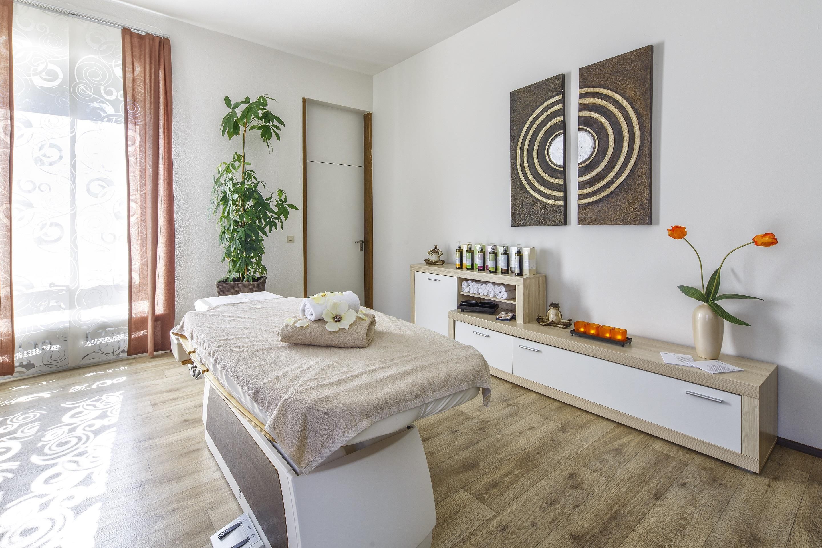 Quarto de hotel com cama, mesa de cabeceira com produtos de higiene, planta em vaso e obra de arte na parede.