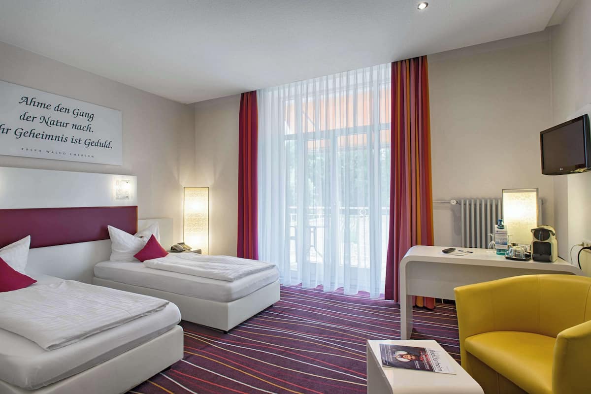 Quarto de hotel com duas camas, uma mesa, uma cadeira e uma televisão.