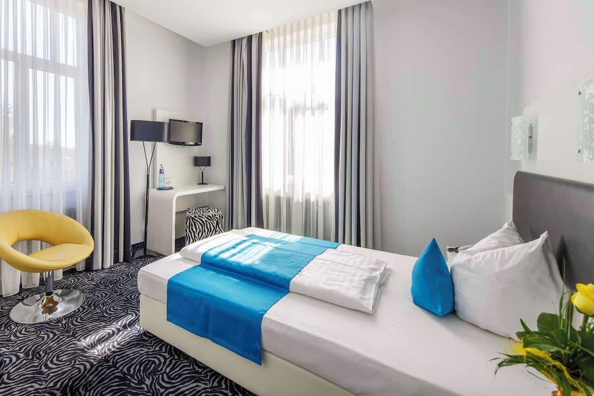 Quarto de hotel com cama, escrivaninha, cadeira e televisão.