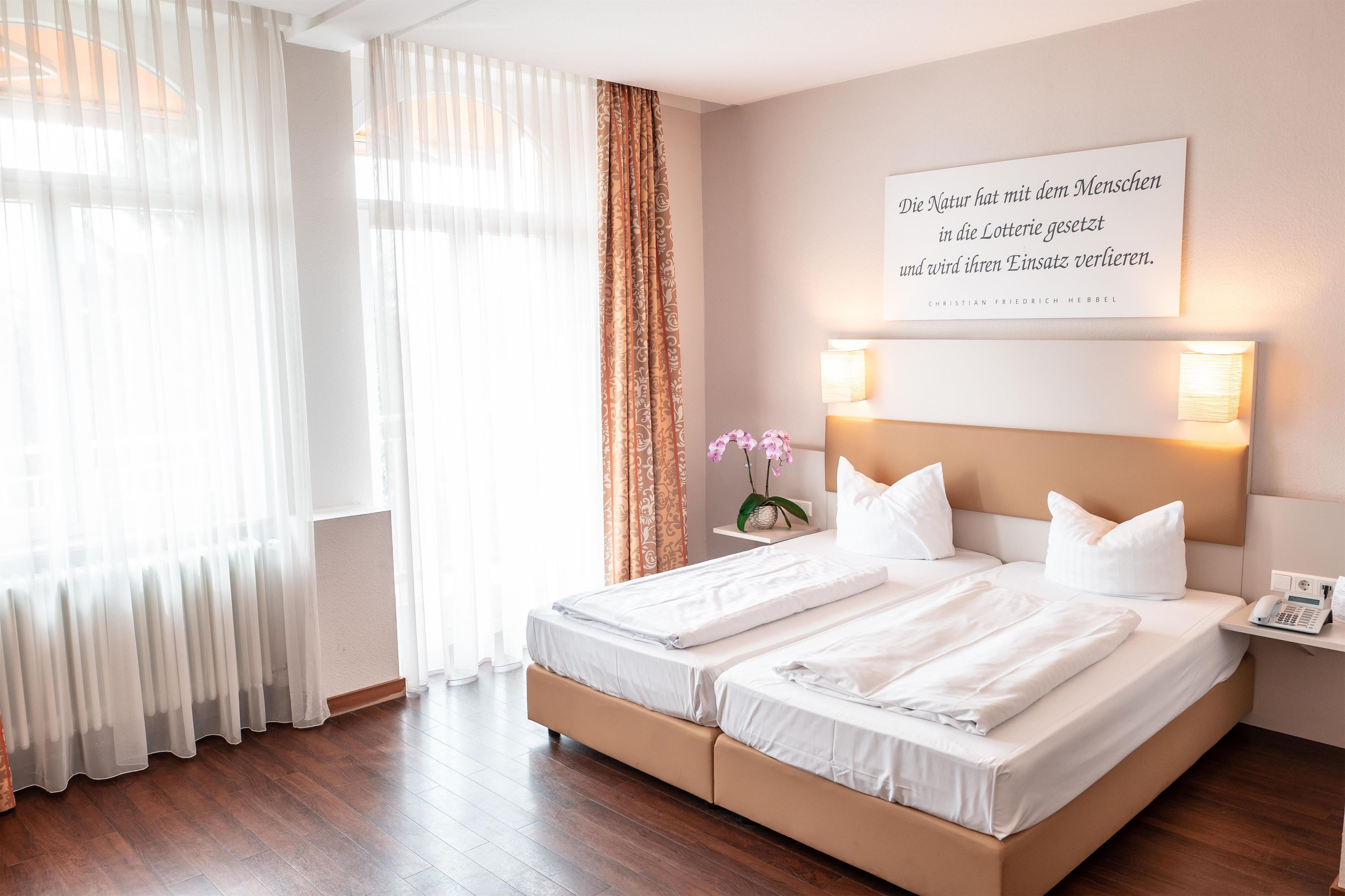Quarto de hotel com cama de casal, mesa de cabeceira com luminária e telefone fixo na parede.