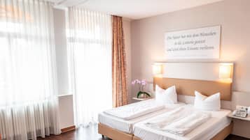 Quarto de hotel com cama de casal, mesa de cabeceira com luminária e telefone fixo na parede.