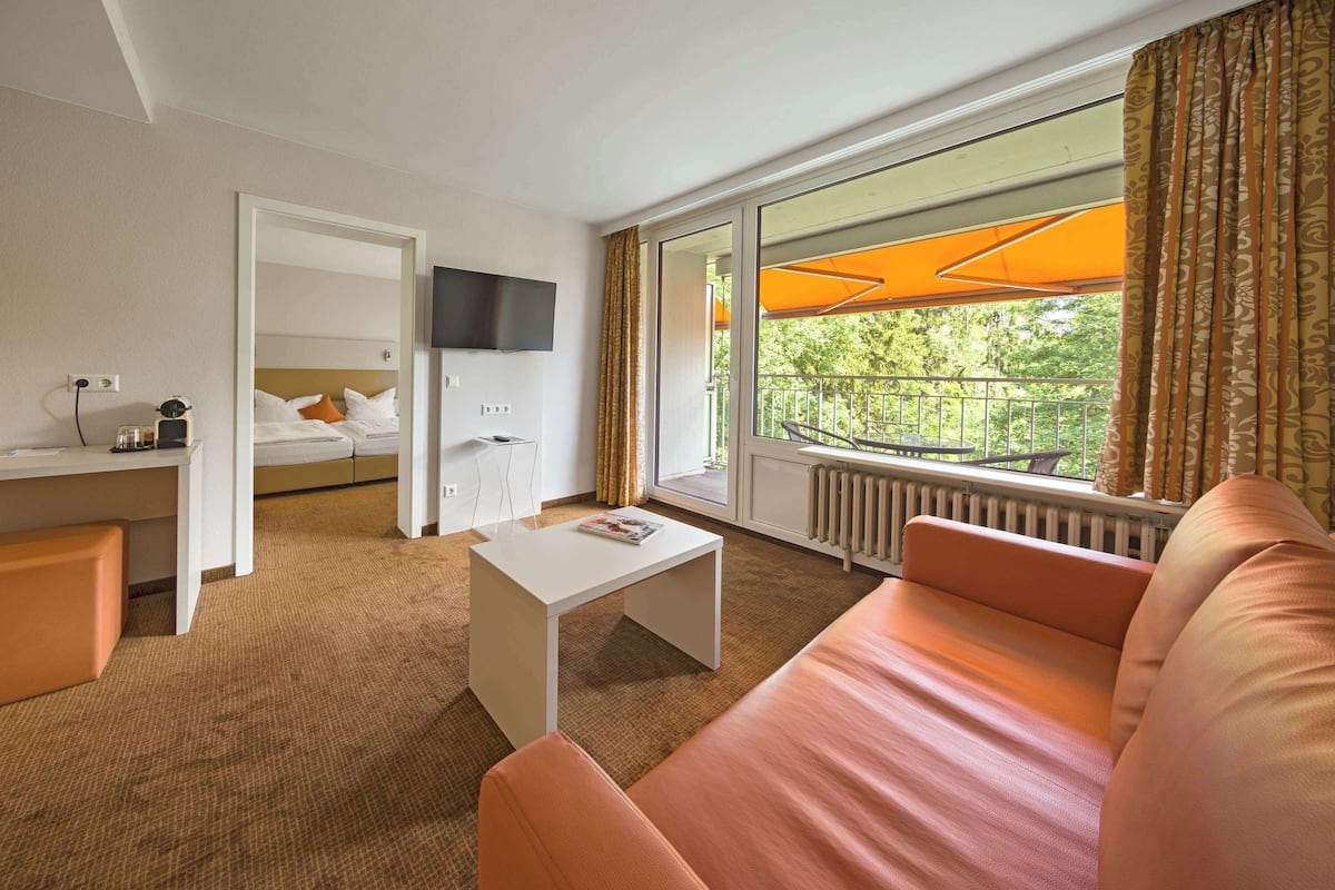 Quarto de hotel com cama, televisão, escrivaninha, mesa de centro e sofá.
