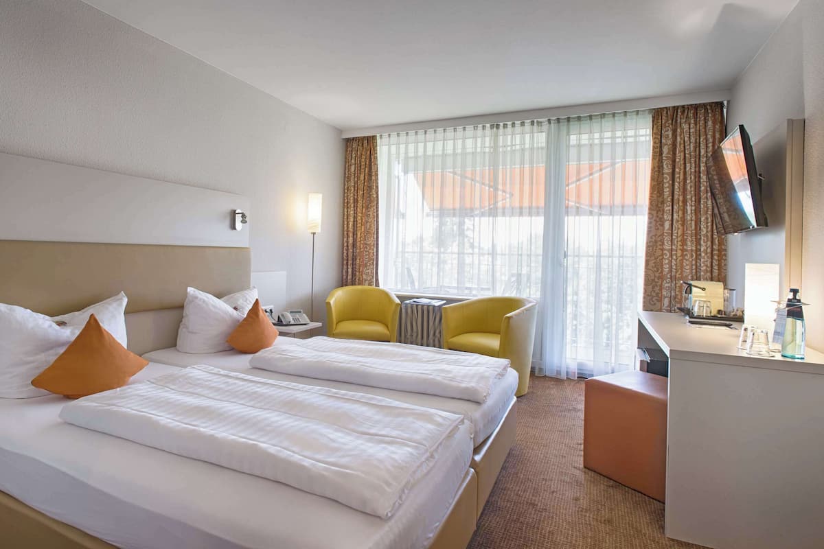 Quarto de hotel com duas camas, uma escrivaninha, uma cadeira, uma televisão e uma janela com cortinas.
