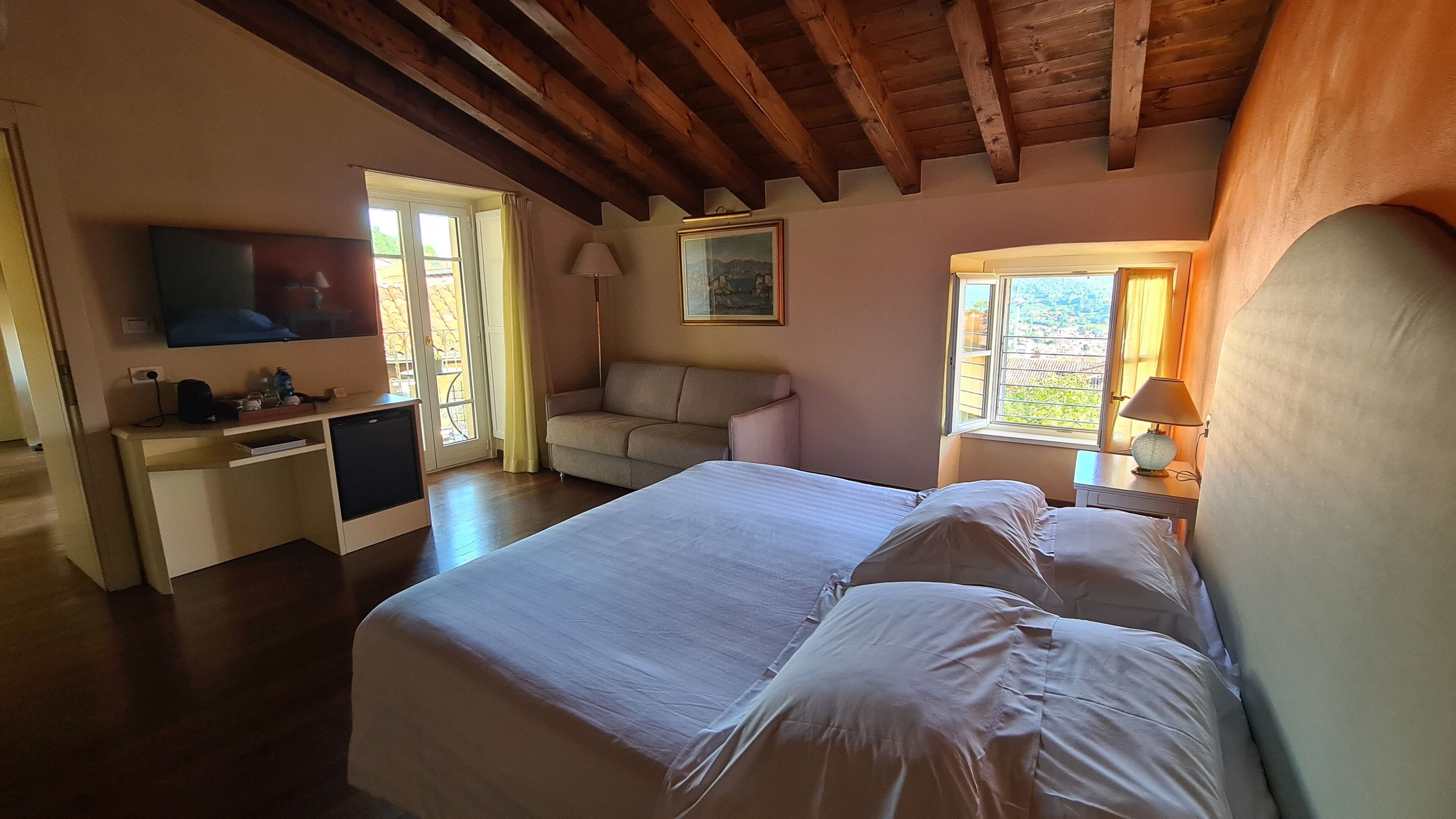 Quarto com cama, escrivaninha, televisão e janela com cortinas.