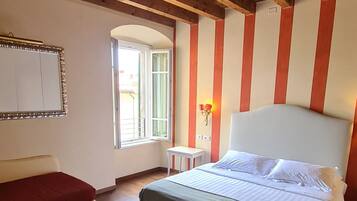 Quarto com teto de madeira, cama com roupa de cama branca, sofá vermelho, mesa pequena e janela com cortinas.