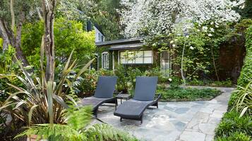 Um jardim com duas espreguiçadeiras, um caminho de pedra e vegetação exuberante.