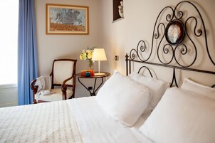 Quarto de hotel com uma cama grande, uma cadeira, uma mesinha com abajur e um quadro na parede.
