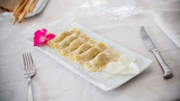 Prato de ravioli com uma flor rosa sobre um prato branco, um garfo, uma faca e um copo de água em uma mesa.