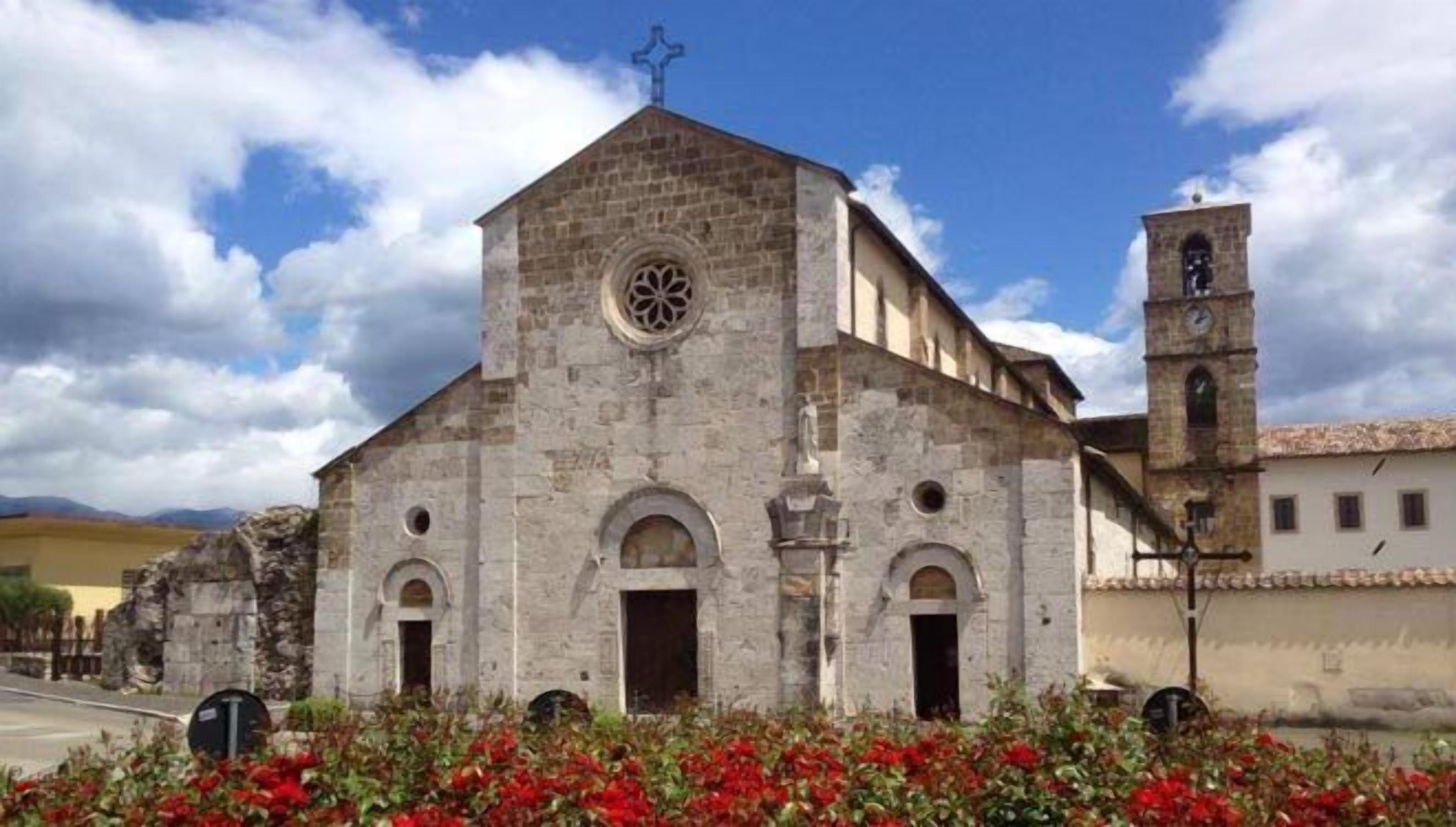 Uma igreja de pedra histórica com uma torre de sino, janelas em arco e uma cruz no topo.