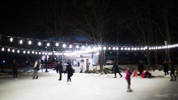 Uma pista de patinação no gelo ao ar livre à noite, com pessoas patinando e um quiosque de comida ao fundo.