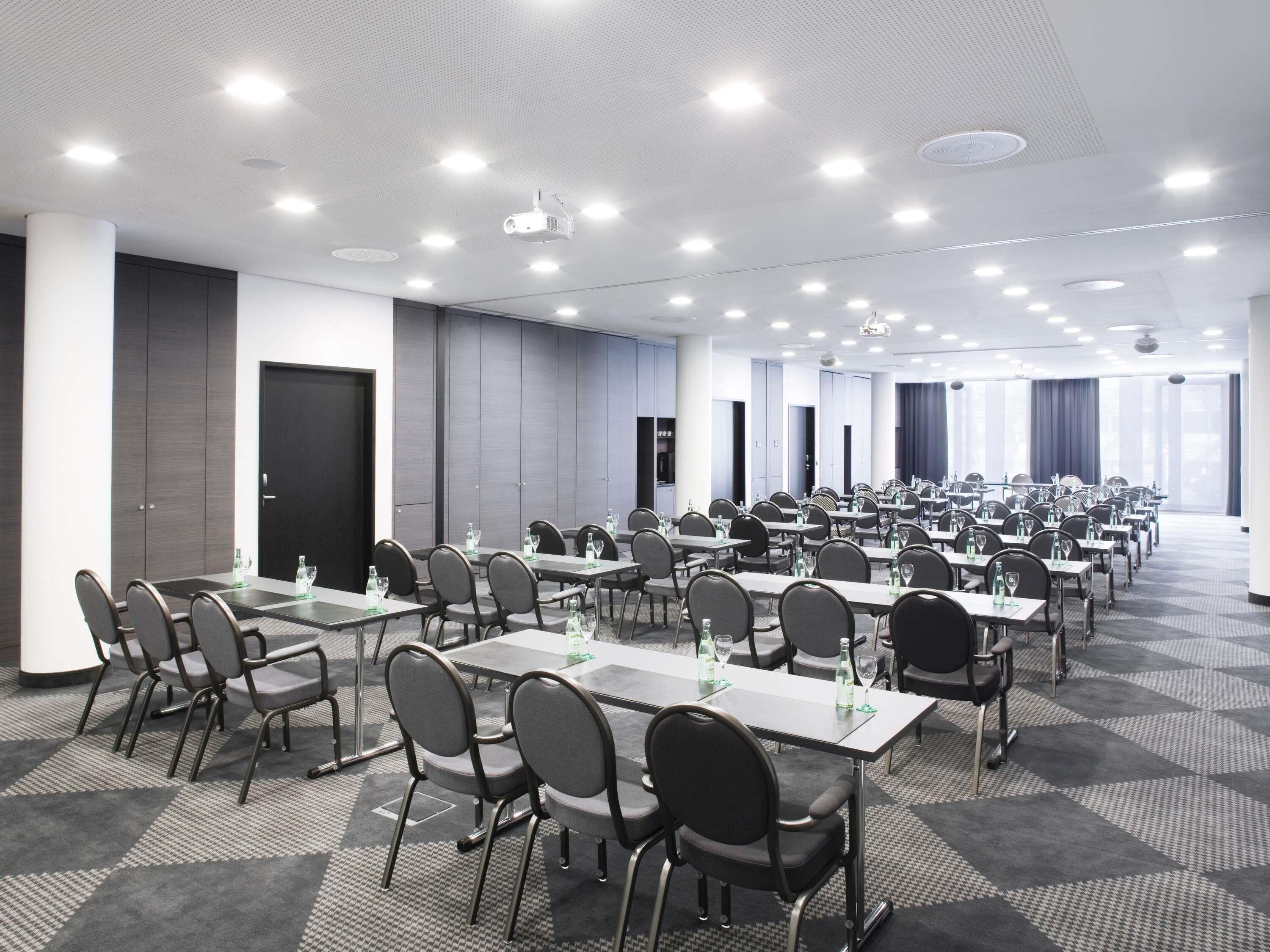 Uma sala de conferências com mesas, cadeiras e um projetor.
